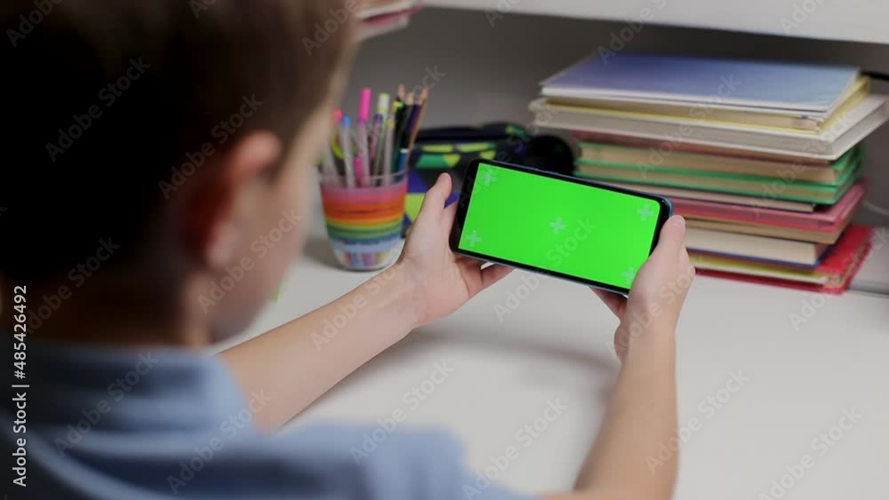 Boy holding a smartphone with a green screen at home, scrolling ...