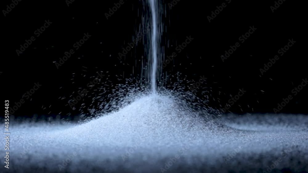Particles of white dry sand are pouring down forming a hill on an ...