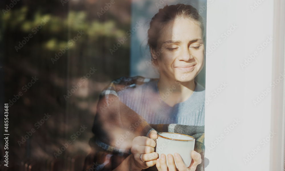 Beautiful young woman drinking morning tea or coffee while sitting by ...