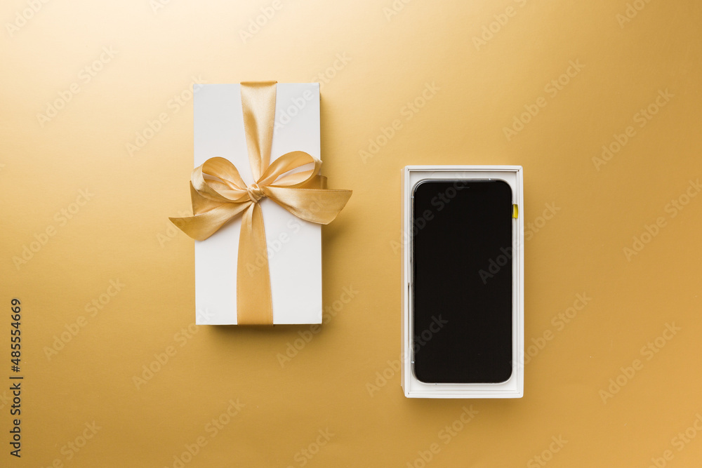 Opened gift box with gold ribbon and smartphone on color background ...