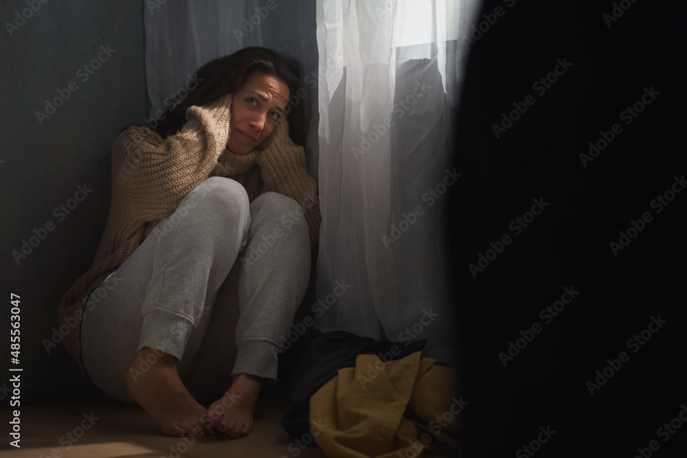Scared woman sitting on ground and covering her head in fear of ...