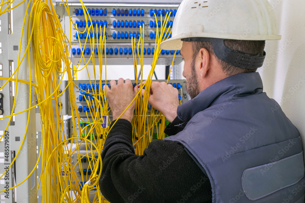 engineer works in data center server room. A man lays fiber optic wires ...