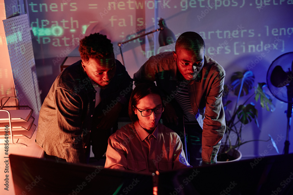 Group of young intercultural programmers bending in front of computer monitors while decoding ...