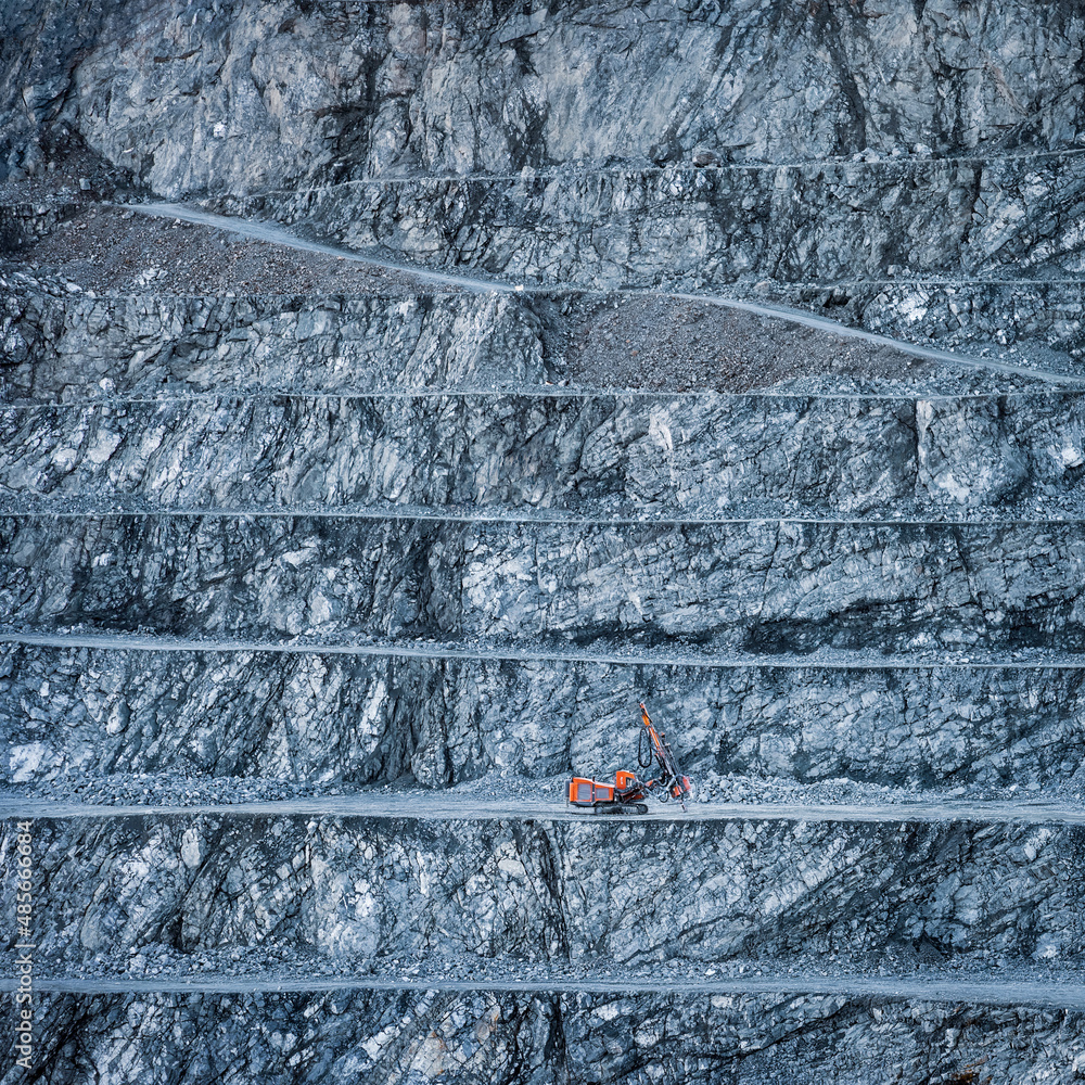 Stepped wall of diabase stone quarry with red drilling rig on a bench ...