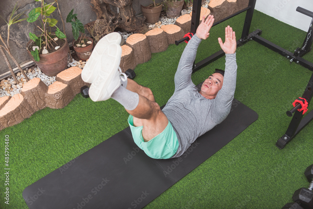 A fit asian man does V-ups with a plate while lying on a black mat ...
