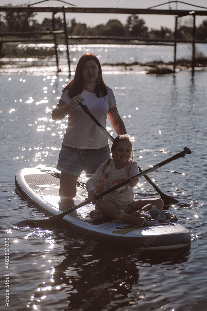 Female child with mother sup boarding with oars in hands smiling and ...