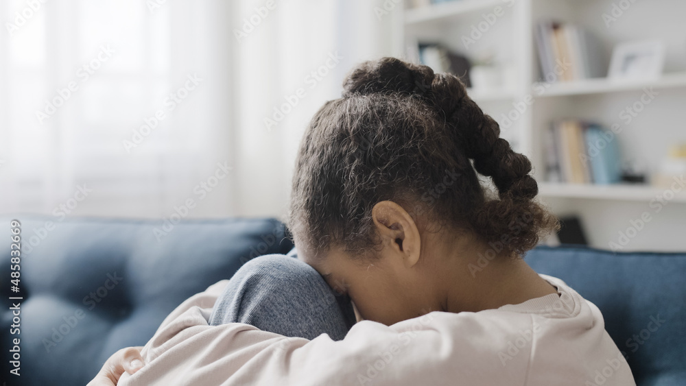 Deeply upset schoolgirl leaning head on her knees, crying, suffering ...