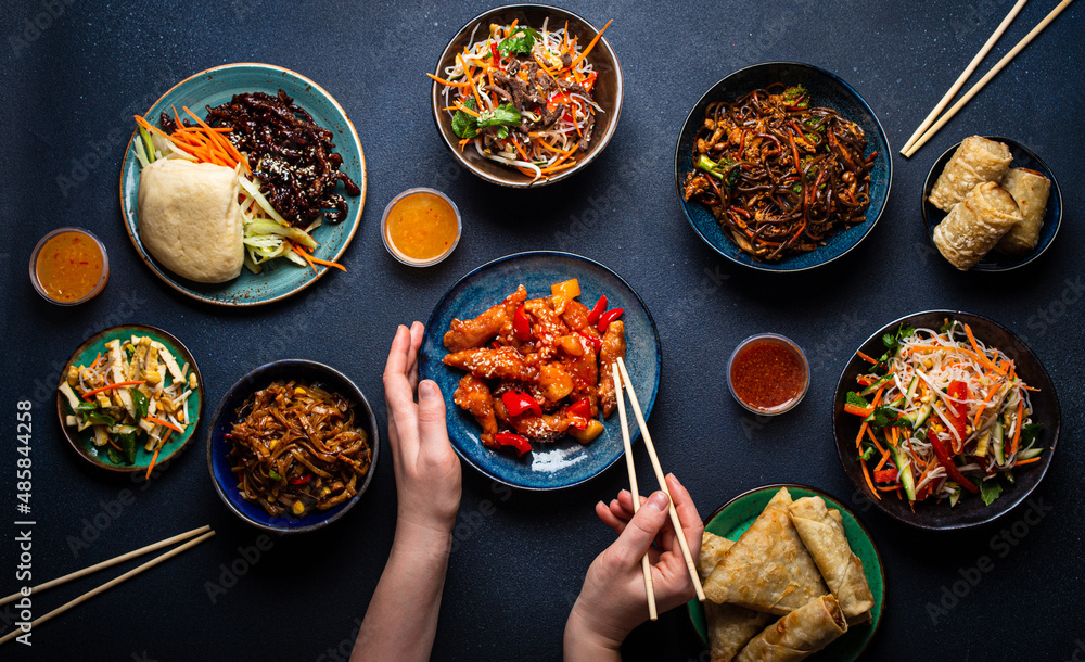 Set of Chinese dishes on table, female hands holding chopsticks: sweet ...