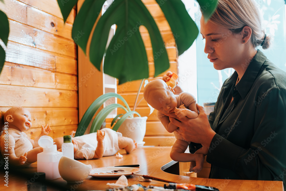 Side view of young woman craftsman decorating realistic dolls of ...