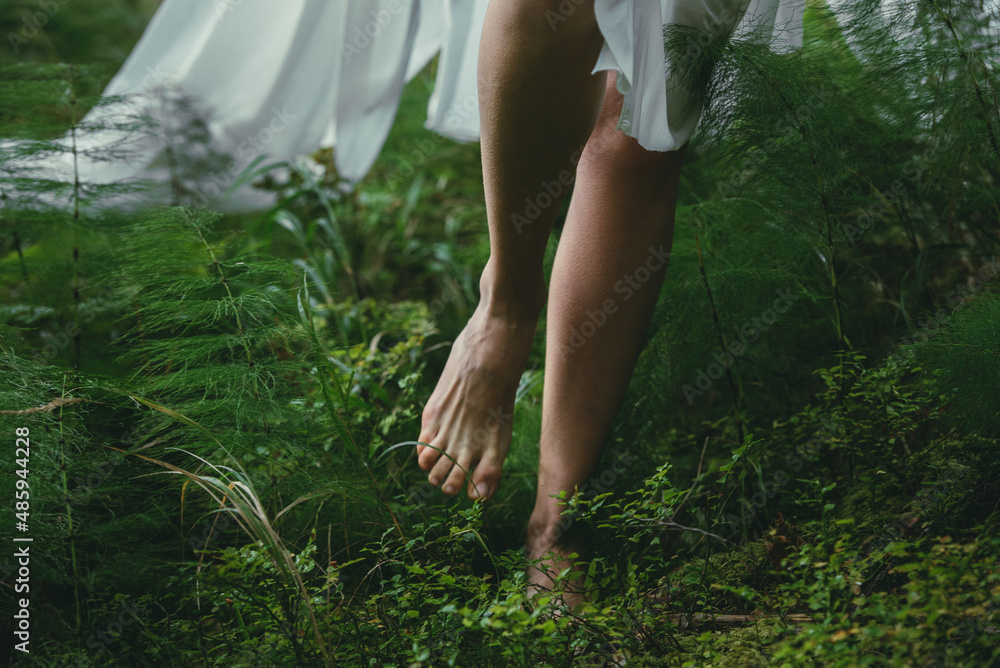 young girl goes barefoot in a white dress on the green grass in the ...
