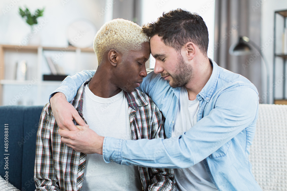 Multi ethnic same sex couple embracing each other while sitting face to ...
