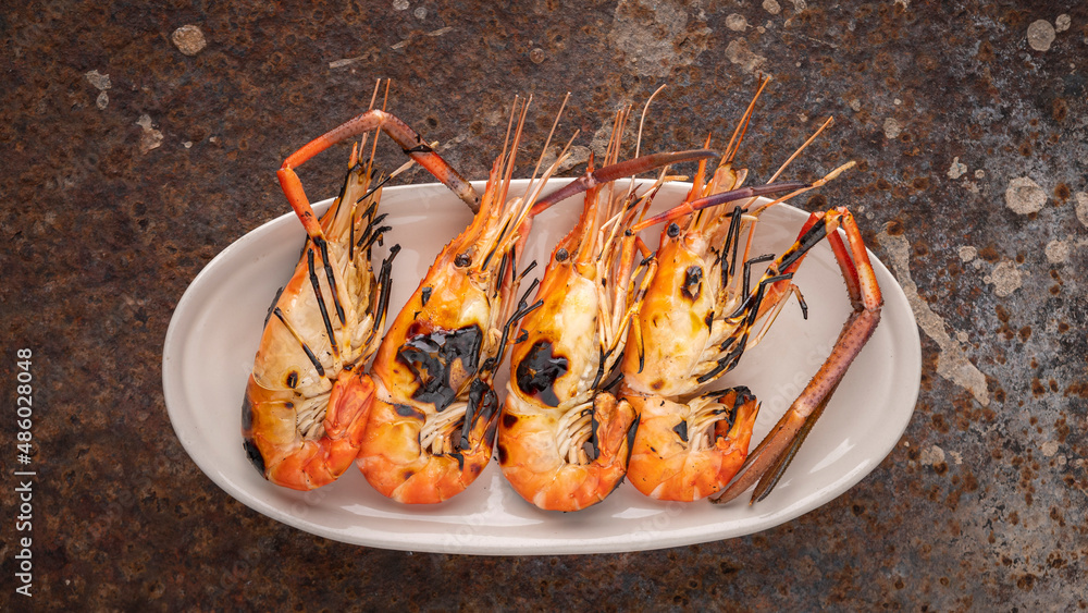 grilled giant freshwater prawns in oval ceramic plate on rusty texture ...