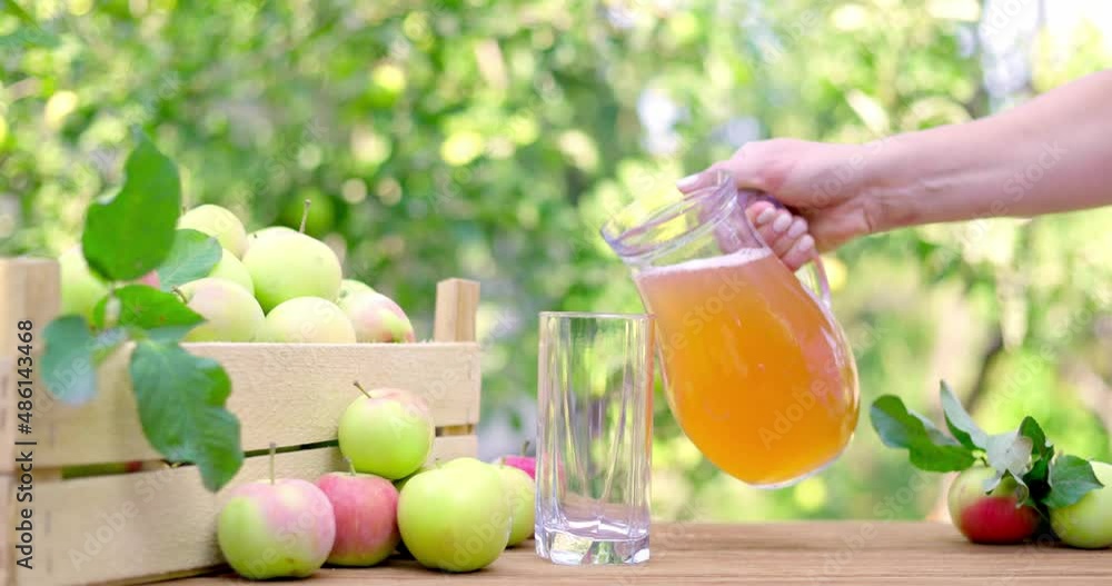 Womans hand is pouring apple juice from a decanter into a glass on the ...