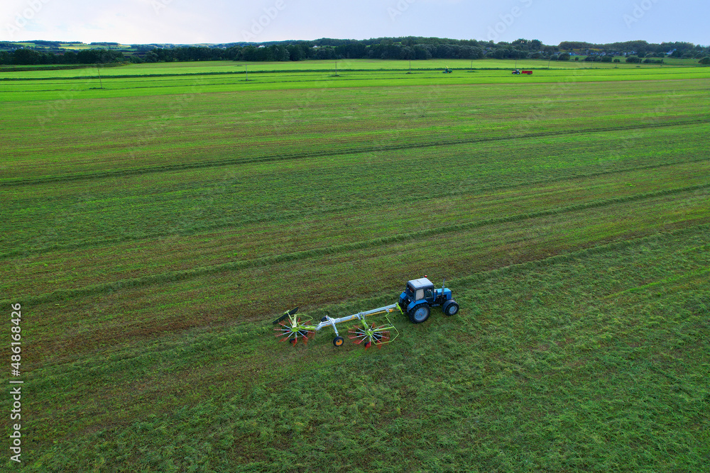 Tractor raking grass for silage harvesting. Agriculture farm machinery ...