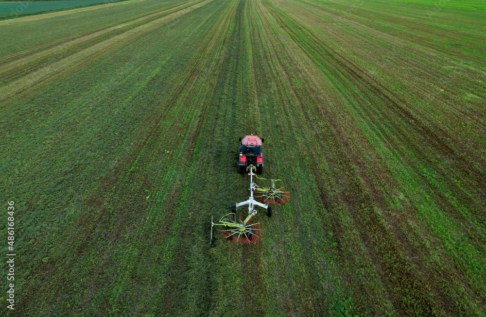 Tractor raking grass for silage harvesting. Agriculture farm machinery ...