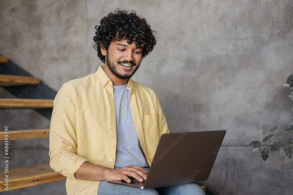 Smiling Indian man using laptop computer typing working freelance ...