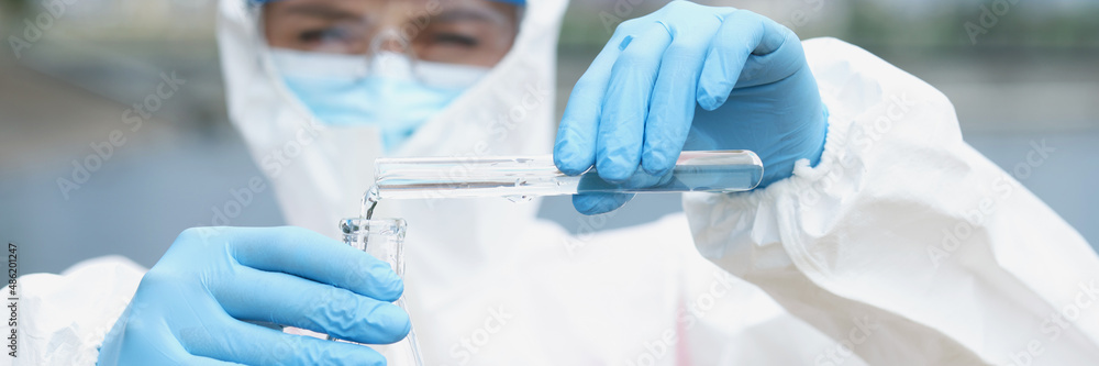 Foto de Researcher in protective suit and glasses with gloves pours ...