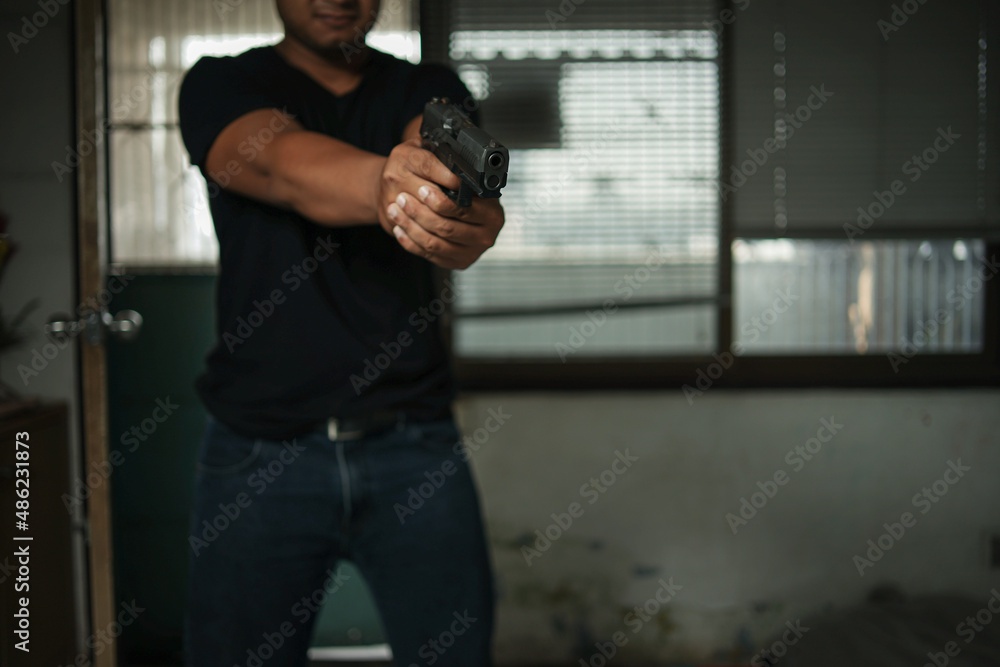 Man holding a pistol, standing in a room in black, pointing and aiming ...