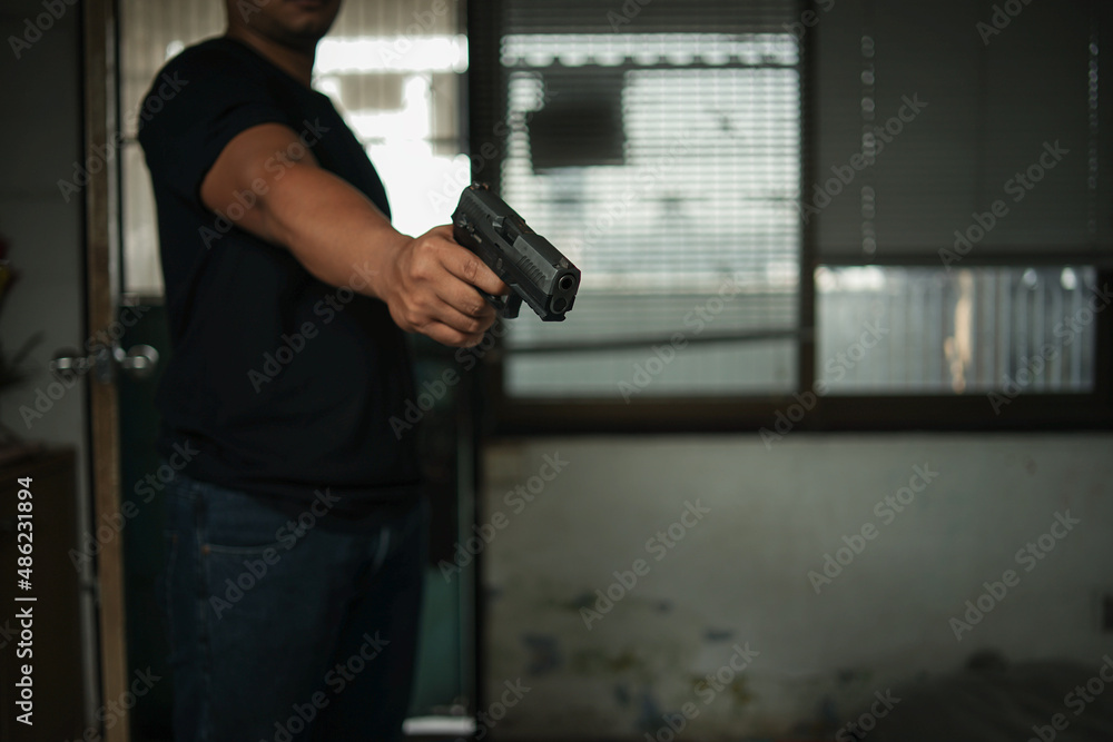 Man holding a pistol, standing in a room in black, pointing and aiming ...
