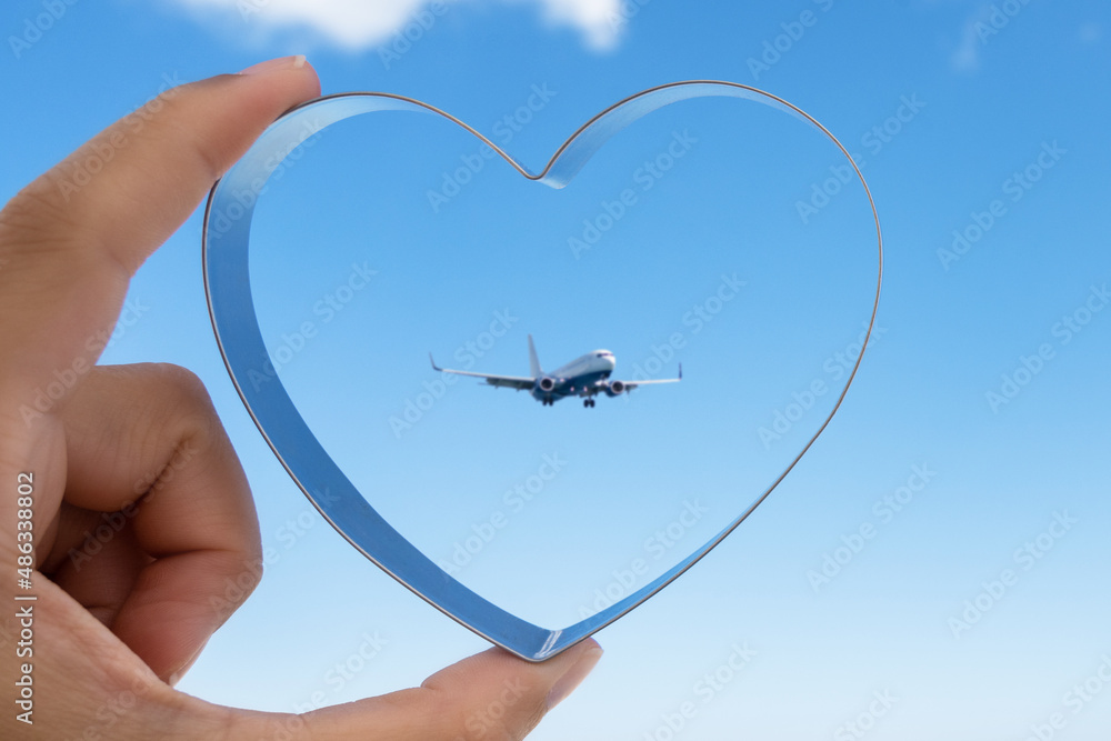 Blue sky and plane with through shape of heart in the female hand ...