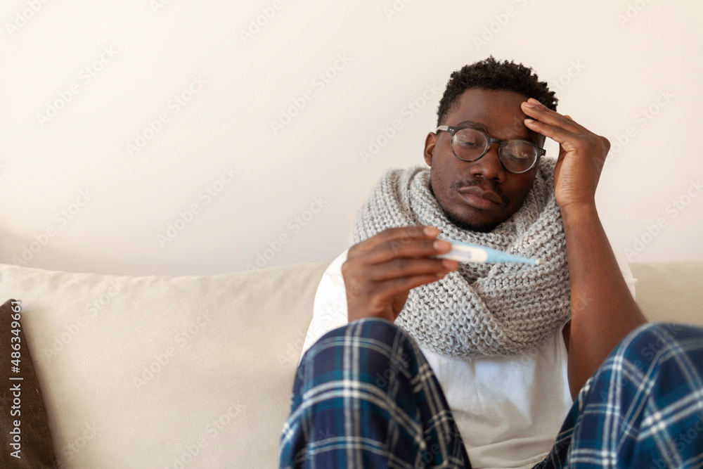 Young sick african guy with fever, checking body temperature with ...