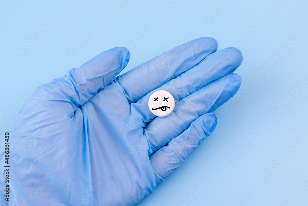 A pill with a dead emoji in a hand in a medical glove on a blue ...