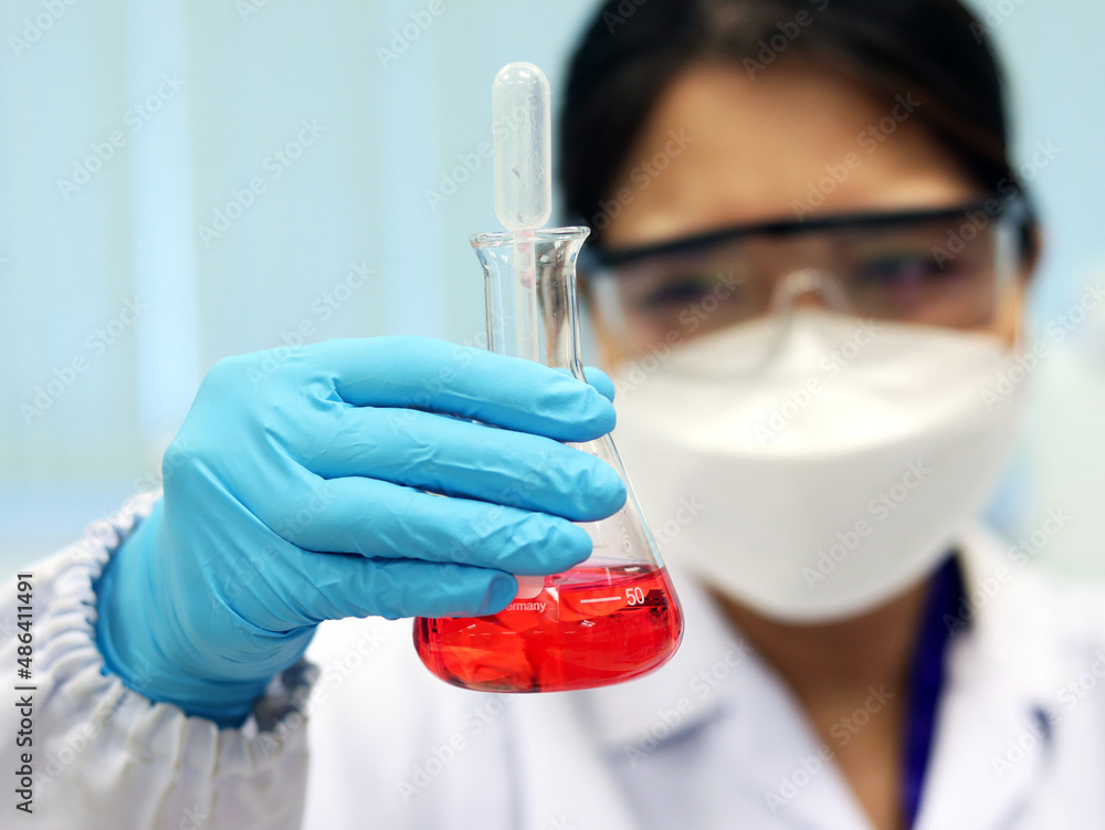 The scientist wears PPE and holds an Erlenmeyer flask laboratory, with ...