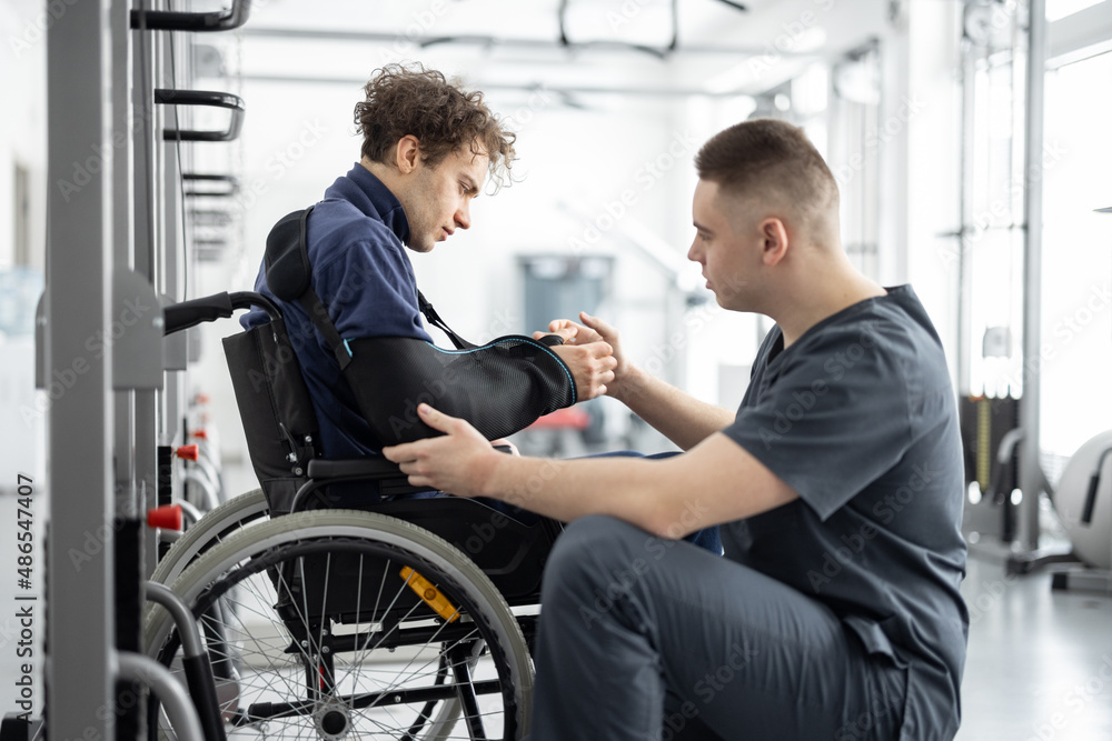 Rehabilitation specialist helps a guy in a wheelchair to do exercises ...