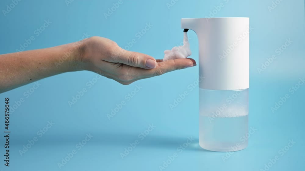 Using an automatic soap dispenser. Young girl woman brings her hands to ...