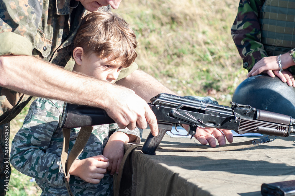 Little boy in military uniform is learning how to disassemble a machine ...