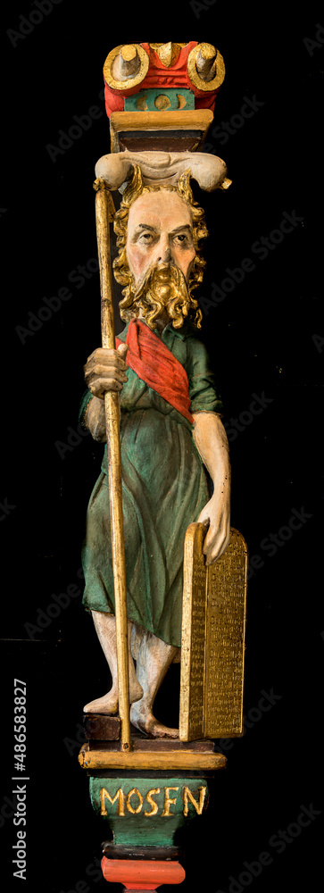 colourful wooden carving depicting Moses on a black background, holding ...