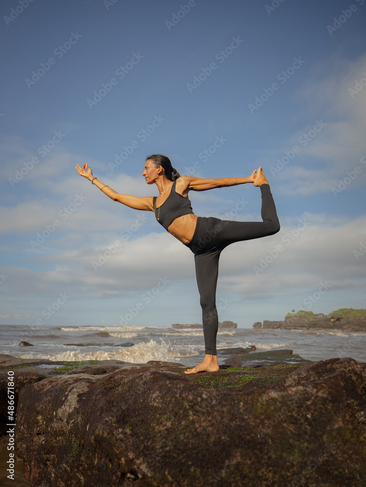 Outdoor morning yoga. Asian woman standing on the rock in Natarajasana ...