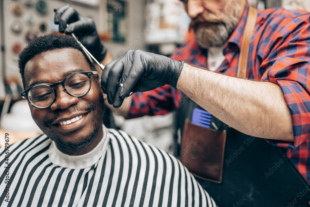 Young African man visiting hairstylist in barber shop. Professional ...