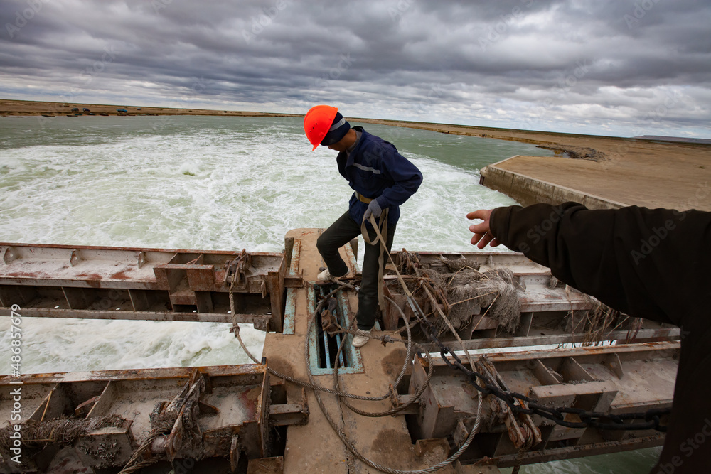 Small Aral Sea Kok-aral dam. Worker in orange hardhat with safety belt ...