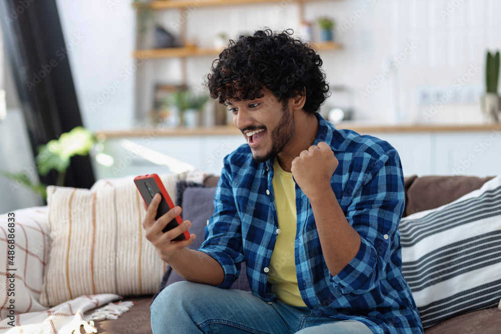 Overjoyed Indian man looking at the screen of mobile phone making yes ...