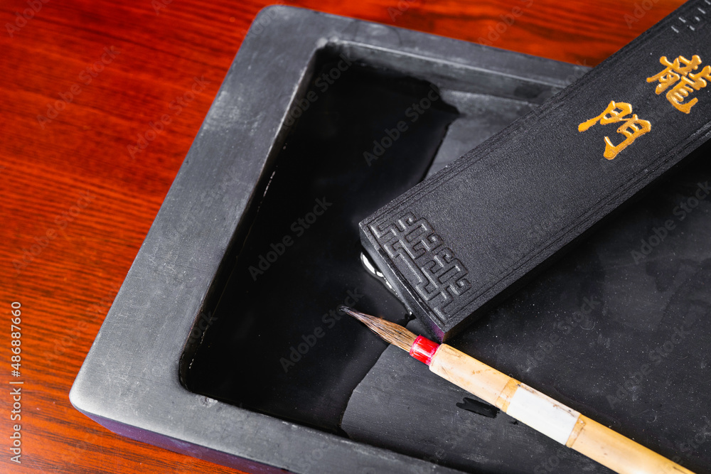 Asian black inkstone, ink bar, and a bamboo brush on a red wood table ...