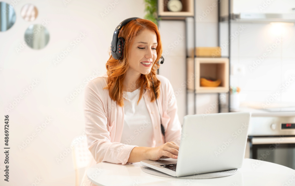Young beautiful redhead woman with headphones having online class or ...