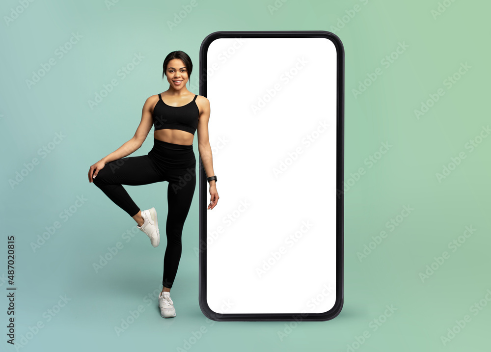 Mobile app for online workout. Young fitness lady standing near huge ...