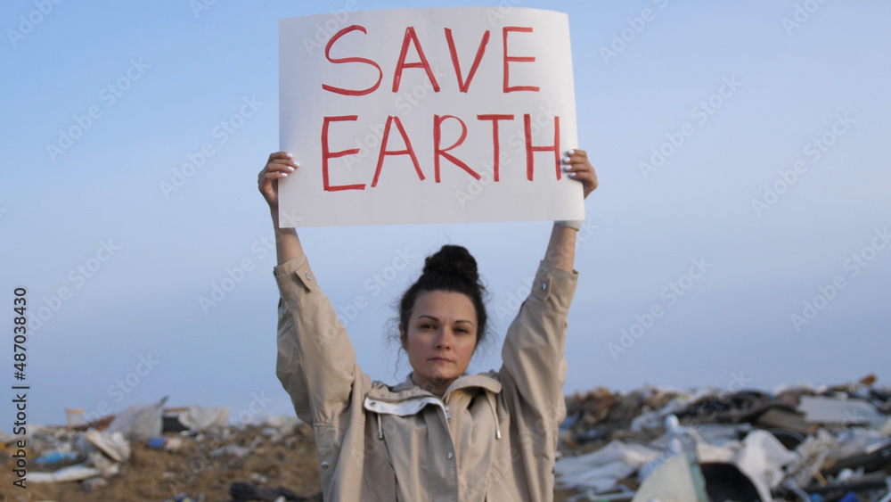 Sad woman volunteer activist stands at big landfill site with garbage ...