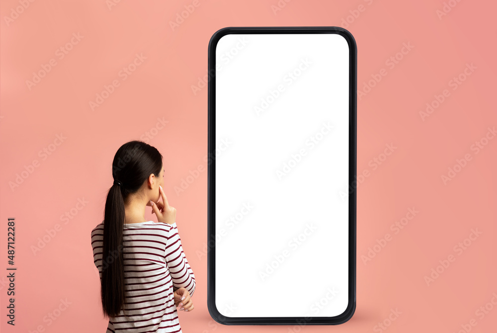 Back view of woman looking at big smartphone with blank white screen ...