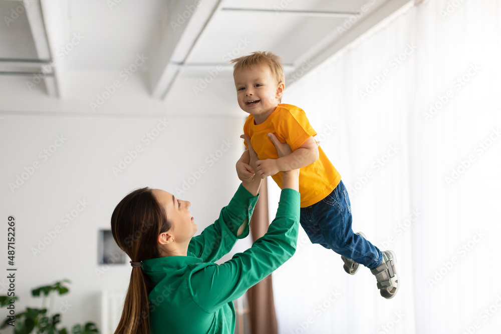 Motherhood concept. Playful lady holding her smiling child boy, lifting ...
