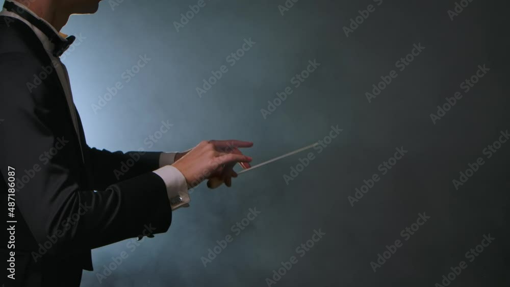 Side view of man gracefully waves conducting baton to synchronize and ...