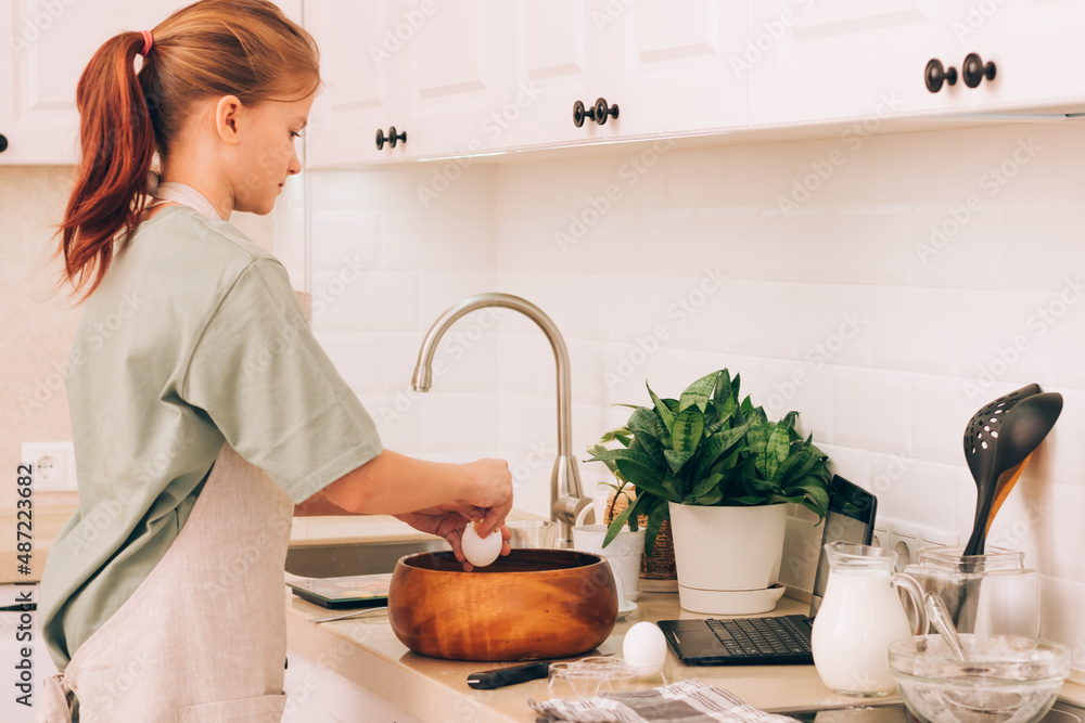 Cute teenage girl in kitchen apron prepares and kneads products for ...