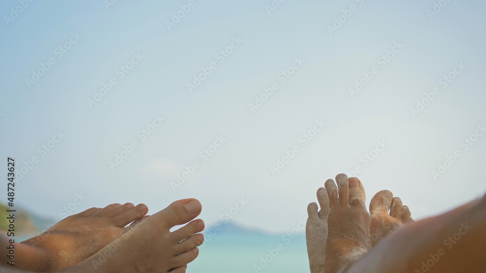 Bare feet of young man and woman couple wiggle lying on beach near calm ...