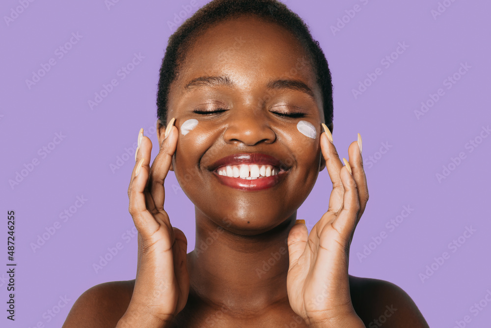 Black african model applying moisturiser face cream to her cheek ...