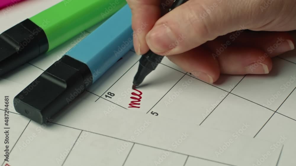 Close up of female hand filling paper calendar with red marker writing ...
