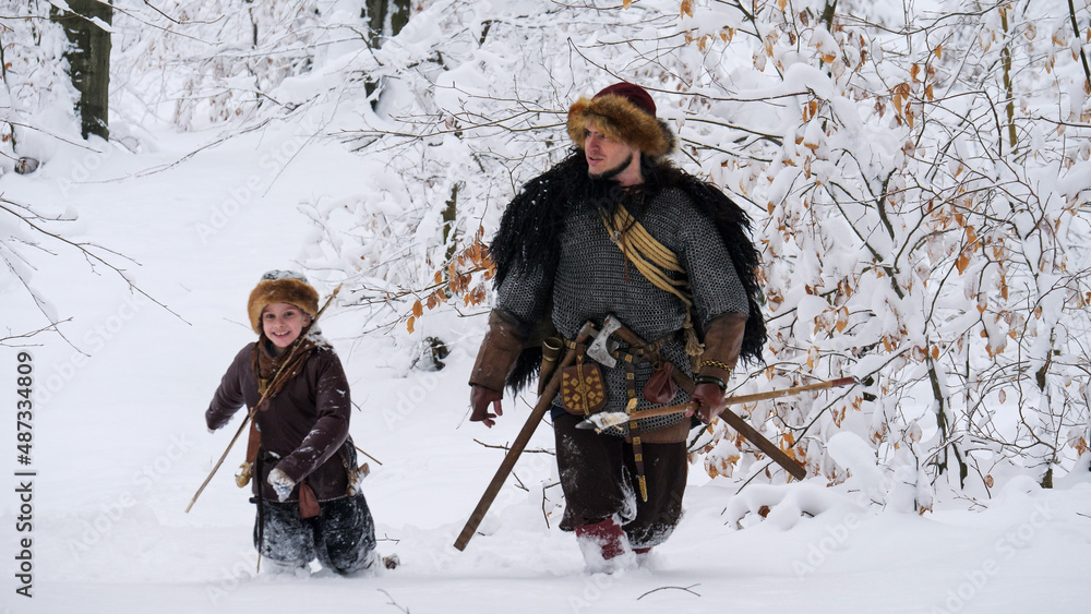 Father viking with his son going in the winter forest, they having axe ...