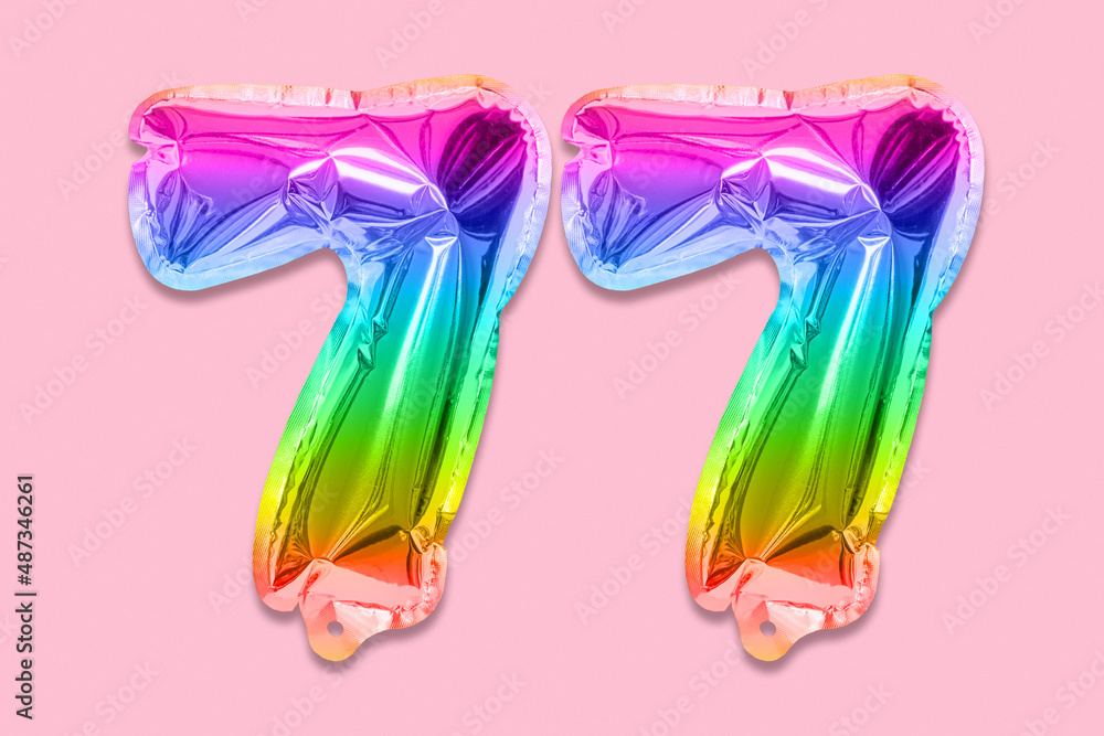 Rainbow foil balloon number, digit seventy seven on a pink background ...