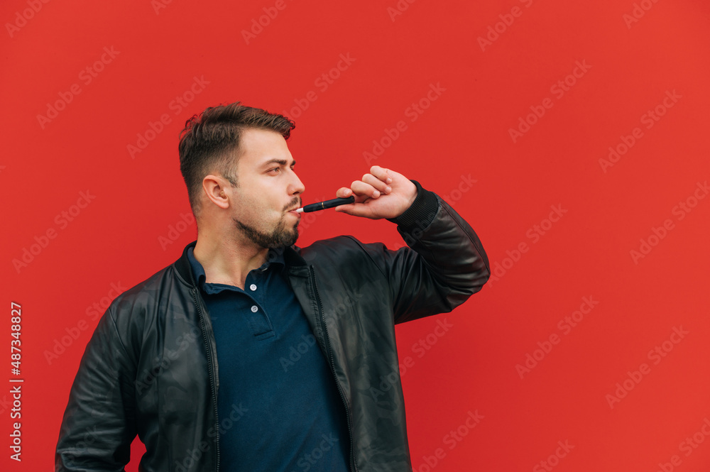 Handsome man in a leather jacket smokes an electronic cigarette ...