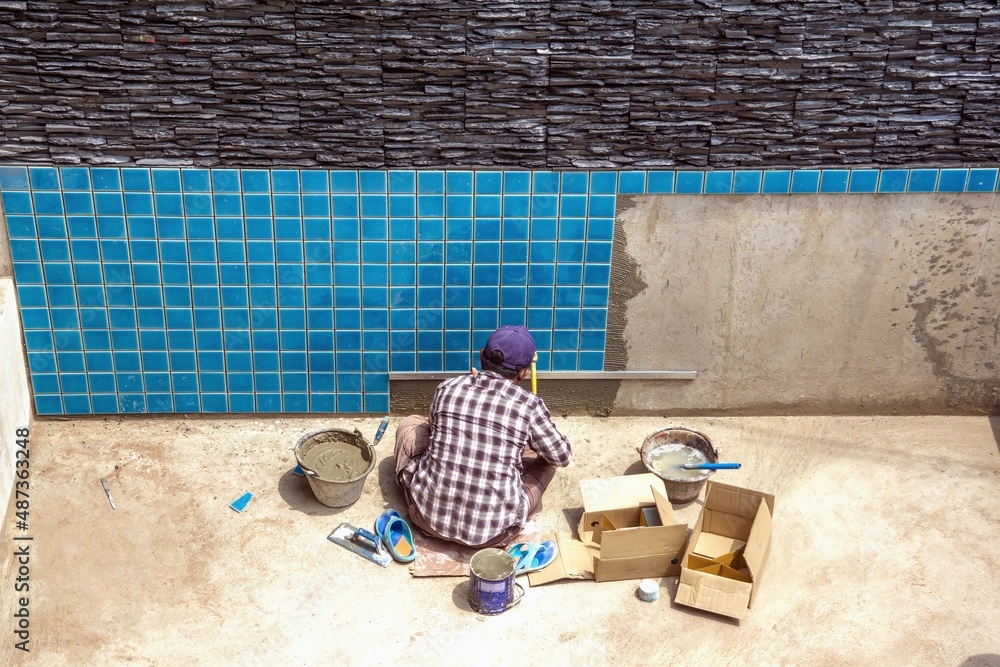 Tiled pool. The man hand while using spacer for installing tiles ...